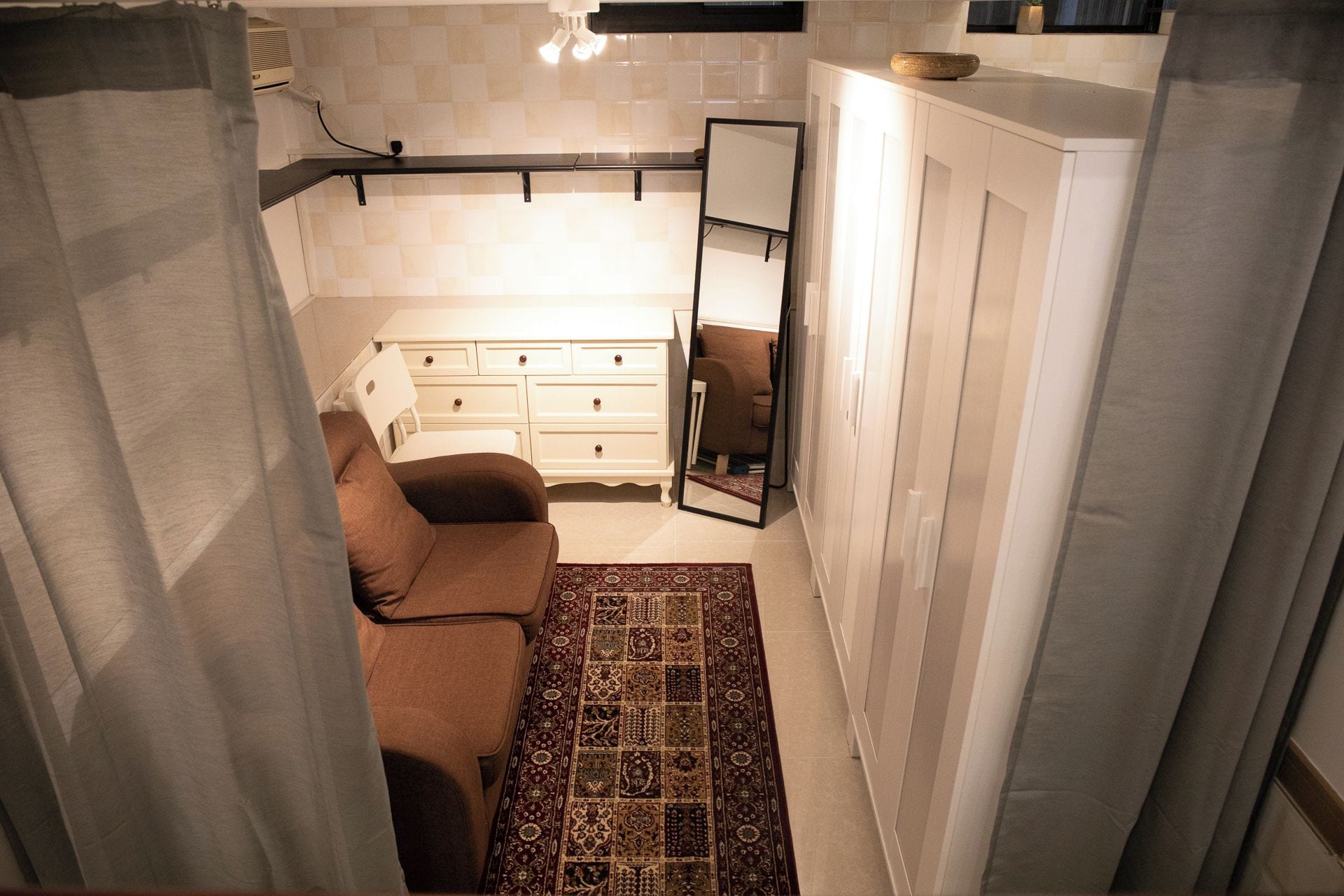 Casa de banho compacta com toucador branco, sofá castanho e tapete estampado.
