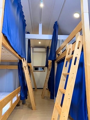 Quarto pequeno com beliches, uma escada, uma janela e uma luminária no teto.