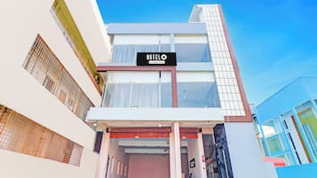 Um hotel moderno com uma placa grande 'HOTEL', fachada de vidro e toldo vermelho sobre a entrada.