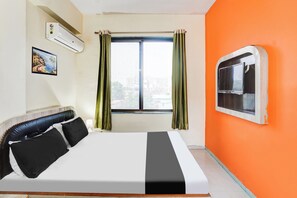 Quarto de hotel com cama, janela com cortinas, ar condicionado, um quadro na parede e televisão fixada na parede.