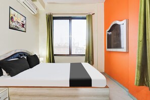 Quarto de hotel com cama, janela com cortinas, um quadro na parede e um ar condicionado.