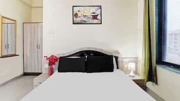 Quarto de hotel com cama, mesa de cabeceira, abajur, vaso com flores, quadro na parede e janela com cortinas.