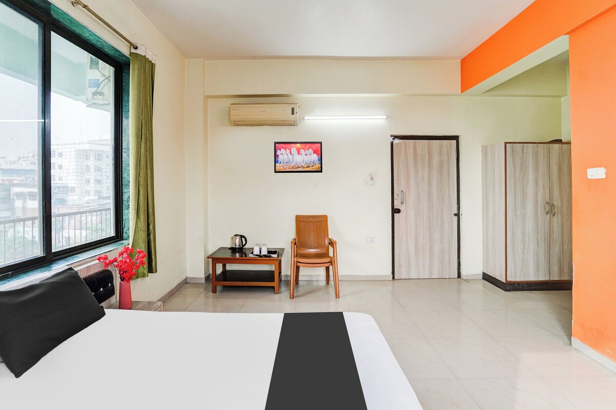 Quarto de hotel com cama, cadeira, mesa com chaleira, um quadro e um guarda-roupa.