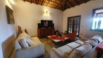 Uma sala de estar com uma televisão sobre um aparador de madeira, uma mesa vermelha e um sofá.