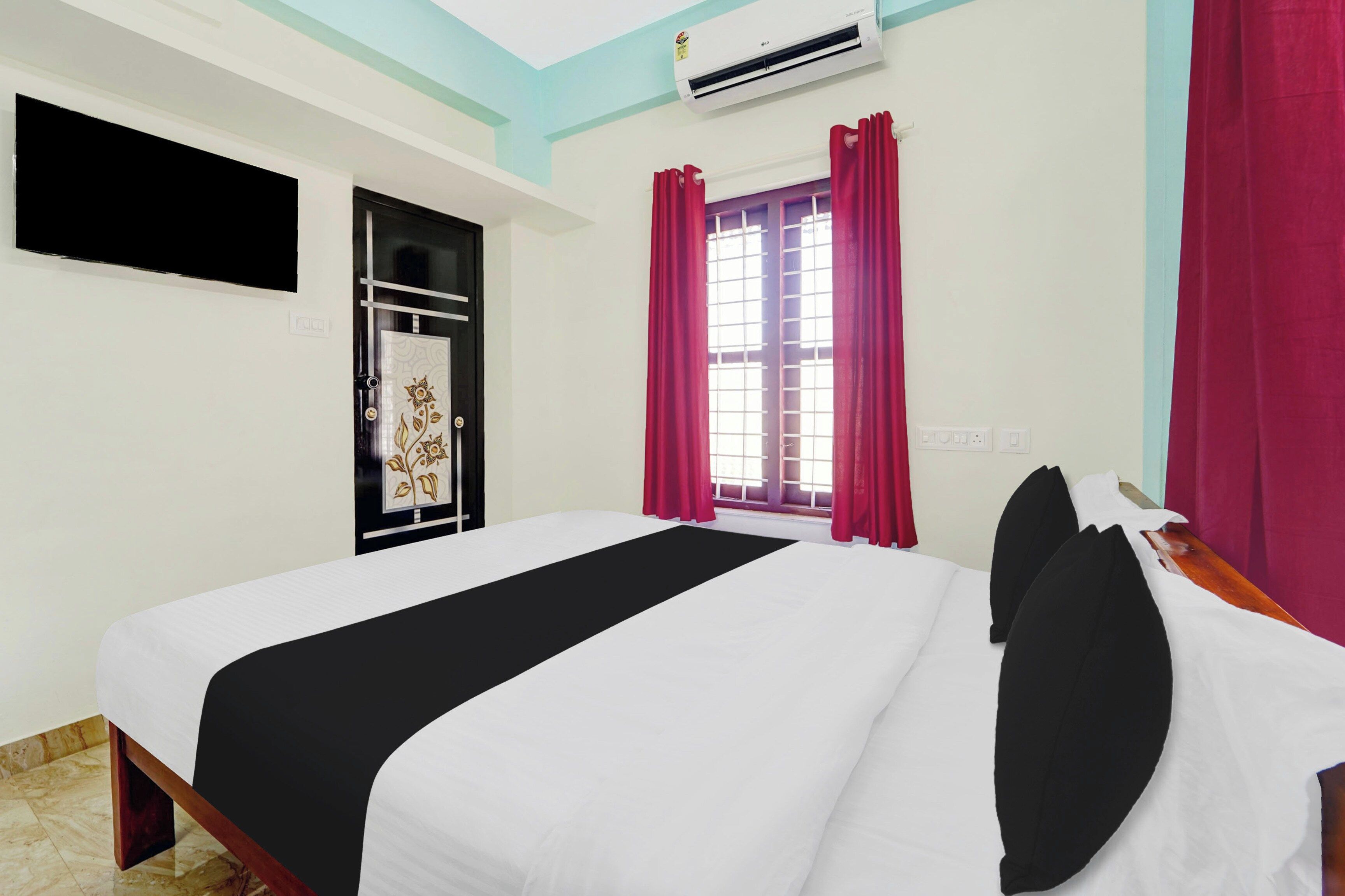 Quarto de hotel com cama, televisão na parede, ar condicionado e janela com cortinas.