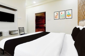 Quarto de hotel com uma cama, uma escrivaninha, uma cadeira, televisão na parede e três quadros emoldurados.