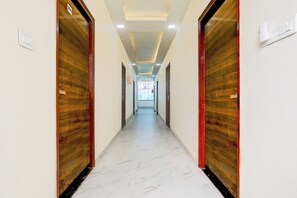 Um corredor com portas de madeira e soalho em azulejos, que leva a uma sala iluminada com uma luminária no teto.