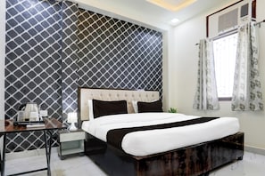 Quarto com cama, mesas de cabeceira, escrivaninha e janela com cortinas.