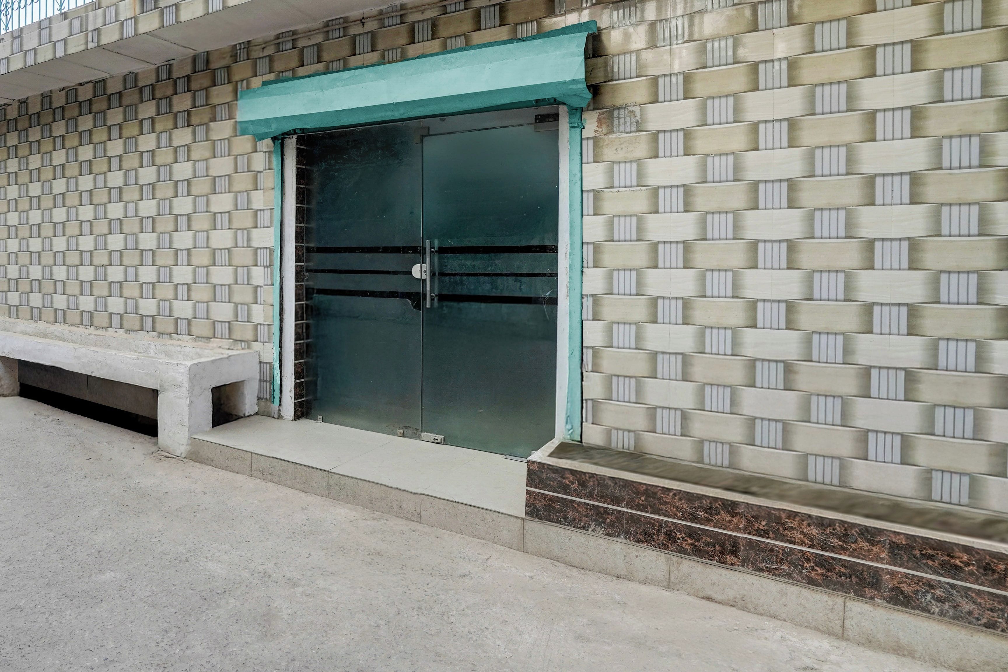 Fachada de edifício com parede de tijolos estampados, toldo verde sobre uma porta de vidro e um banco de concreto.