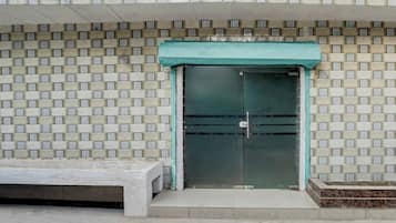 Entrada de um edifício com parede estampada, toldo verde e um banco.
