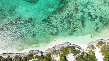 Vista aérea de uma propriedade costeira com piscina, vários edifícios e uma praia.