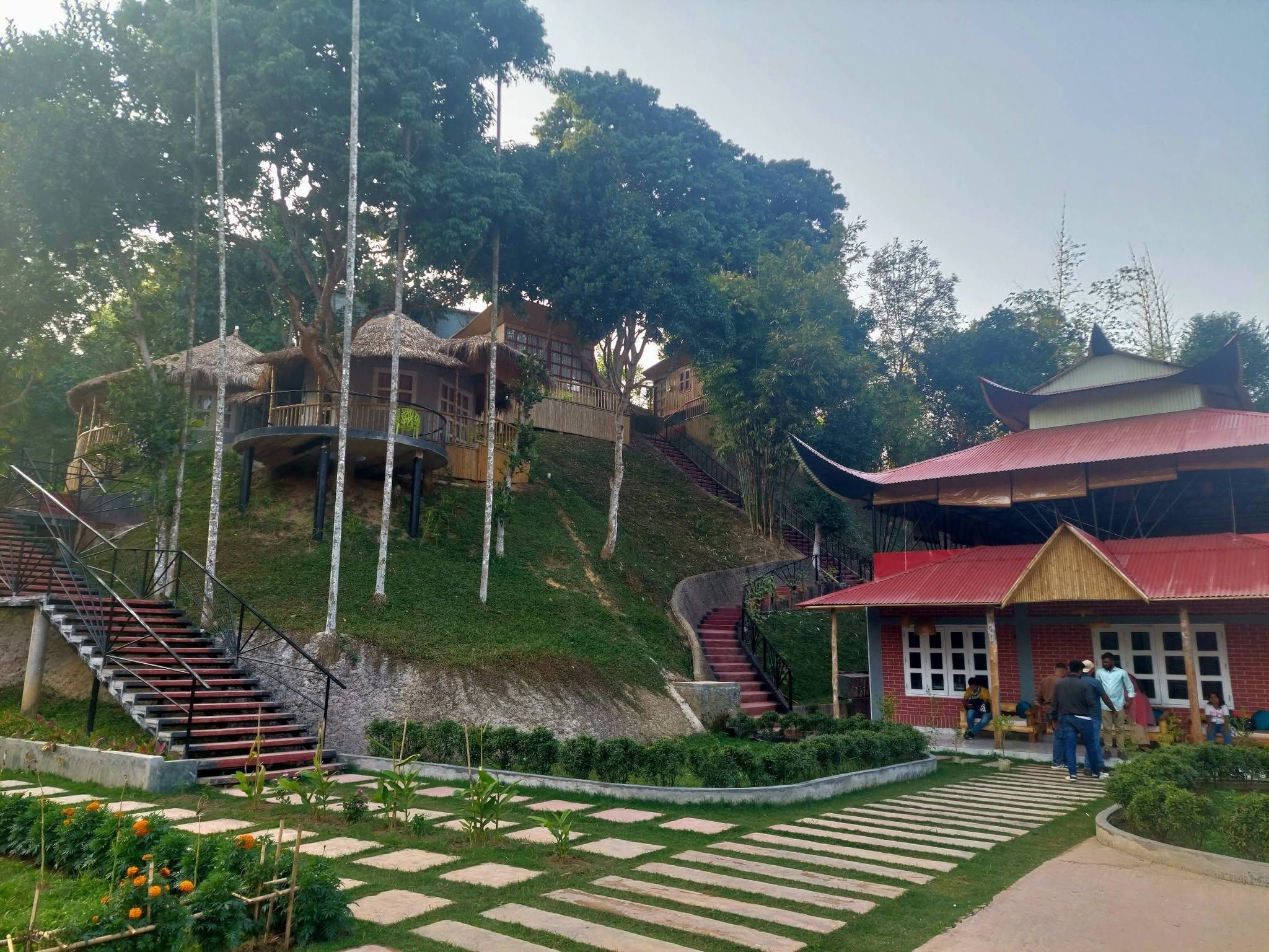 Um resort na encosta de uma colina com vários edifícios, incluindo uma construção com telhado vermelho e varanda, e um prédio com telhado de palha.