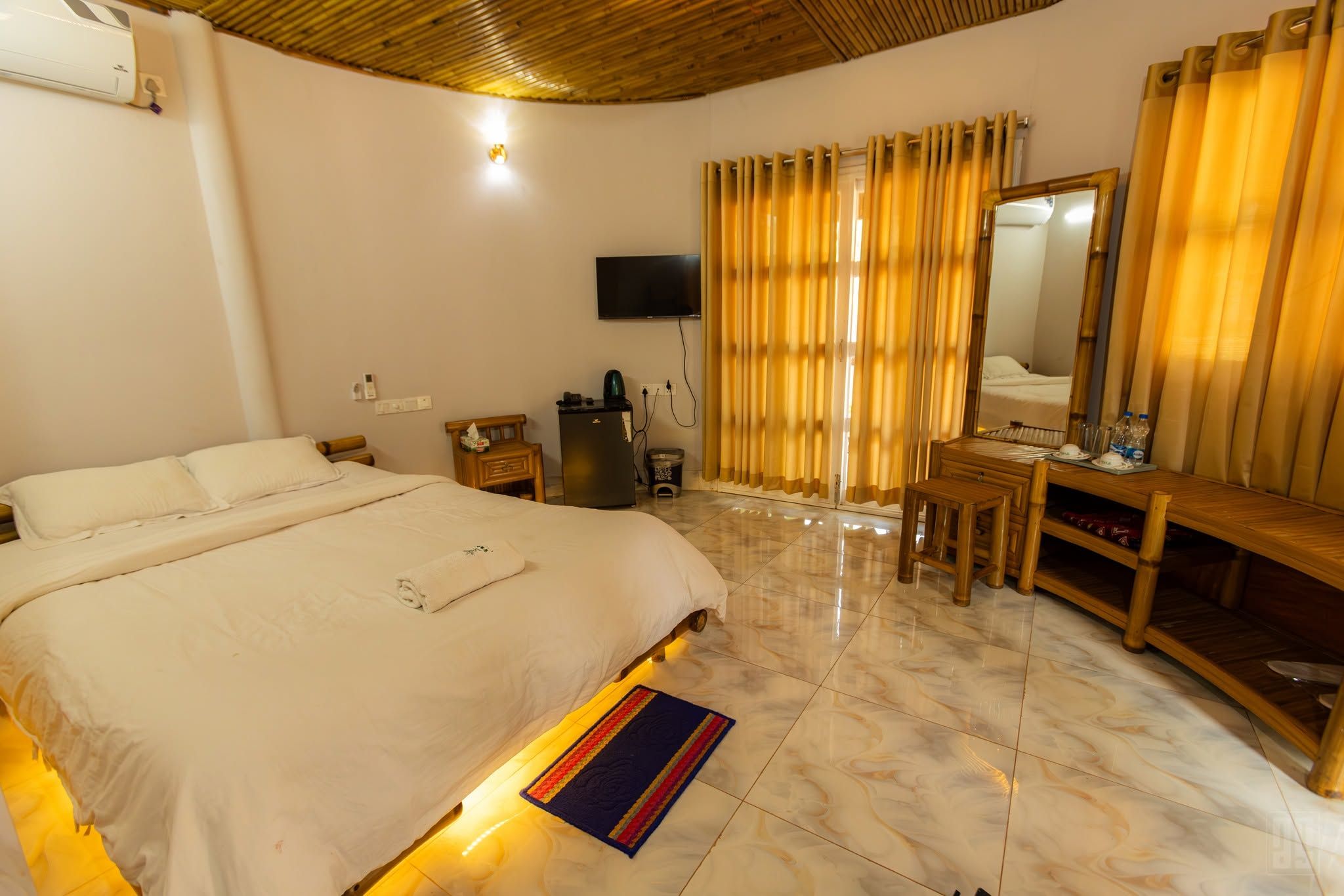 Quarto de hotel com cama, escrivaninha, cadeira, televisão, espelho e janela com cortinas.