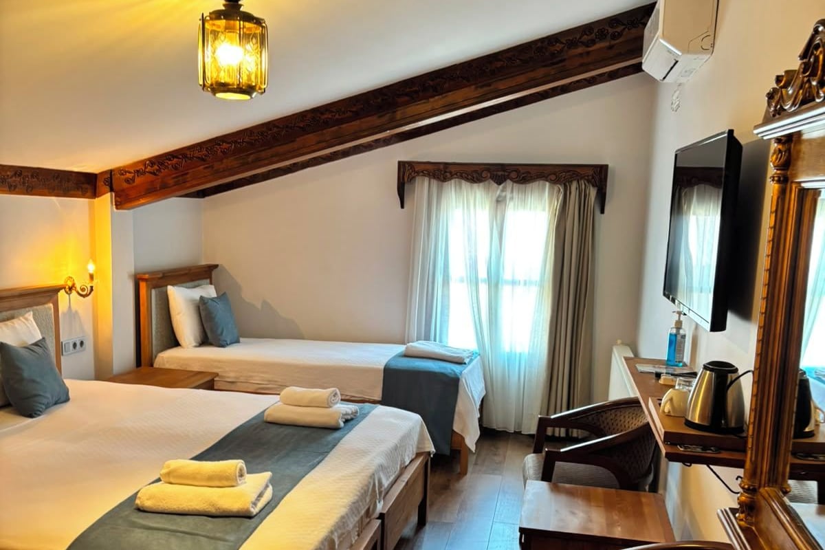 Quarto de hotel com duas camas, uma escrivaninha, uma cadeira, uma televisão e uma luminária de teto.