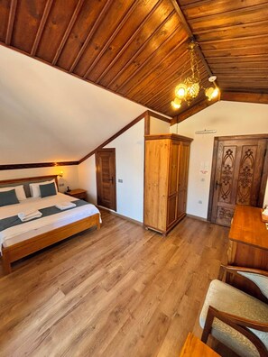Quarto com teto de madeira, uma cama, guarda-roupa e uma escrivaninha com cadeira.