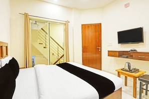 Quarto de hotel com cama, televisão, guarda-roupa de madeira, secretária com chaleira e escada.