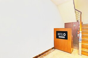 Entrada de um quarto de hotel com porta de madeira identificada como 'HOTELO Company Serviced'.