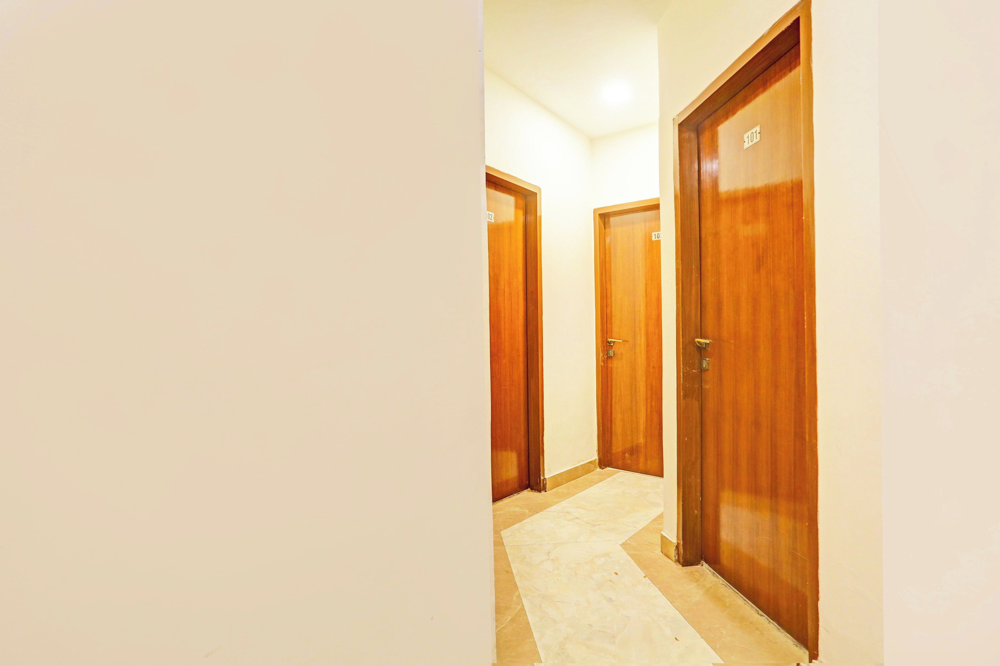 Um corredor com três portas de madeira, cada uma delas identificada com um número. O chão está coberto por um tapete de cor clara.