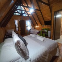 Um quarto de sótão aconchegante, com teto inclinado, cama com almofadas, mesa pequena e televisão na parede.