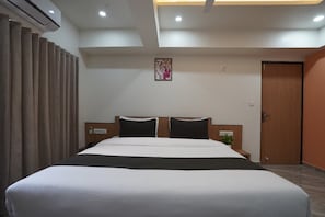 Quarto de hotel com uma cama grande, mesa de cabeceira, ar condicionado, porta e luminária no teto.