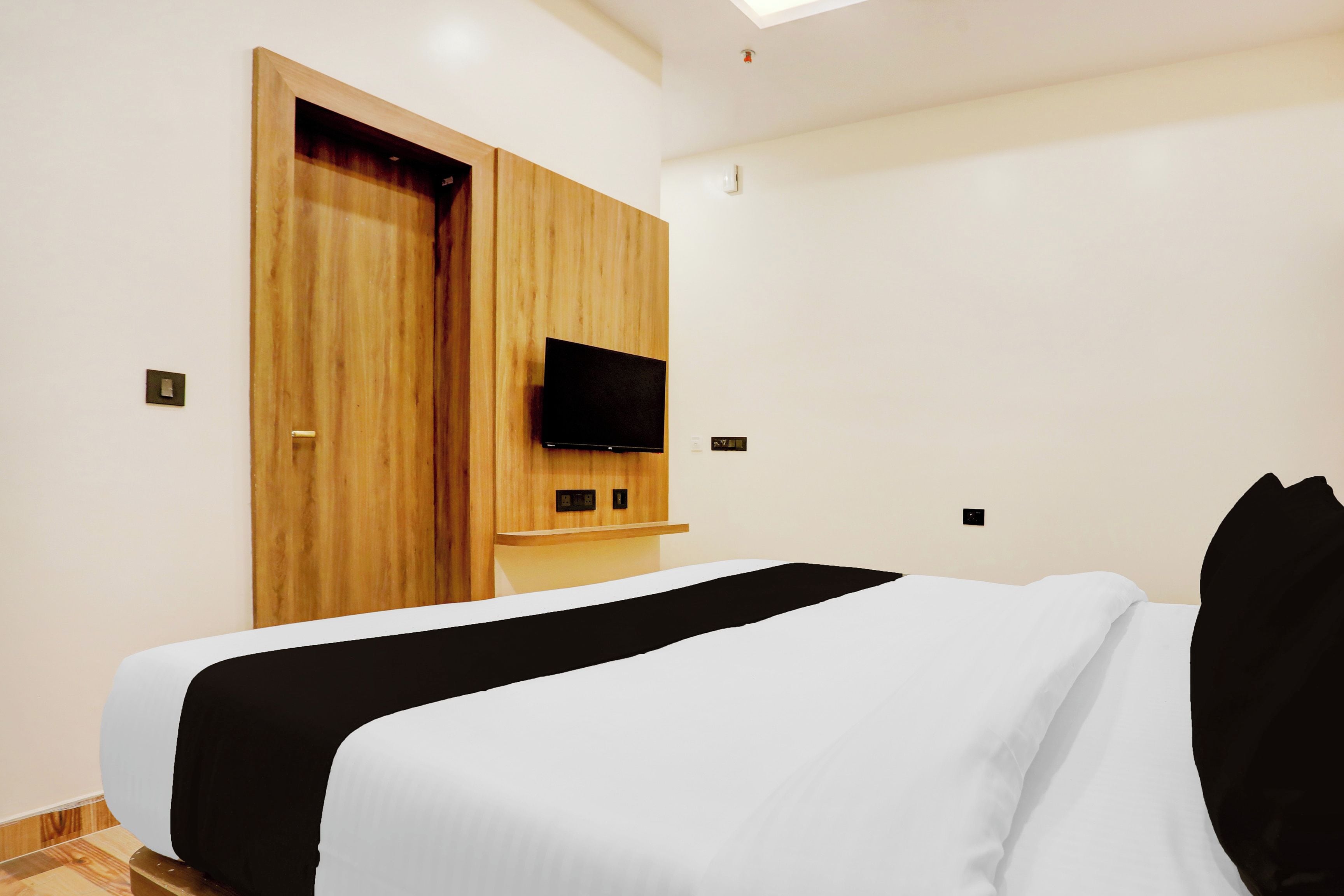 Quarto de hotel com cama, guarda-roupa de madeira, televisão de tela plana na parede e uma mesinha.