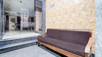 Área de recepção com parede de mármore, um banco e sinalização indicando um elevador.