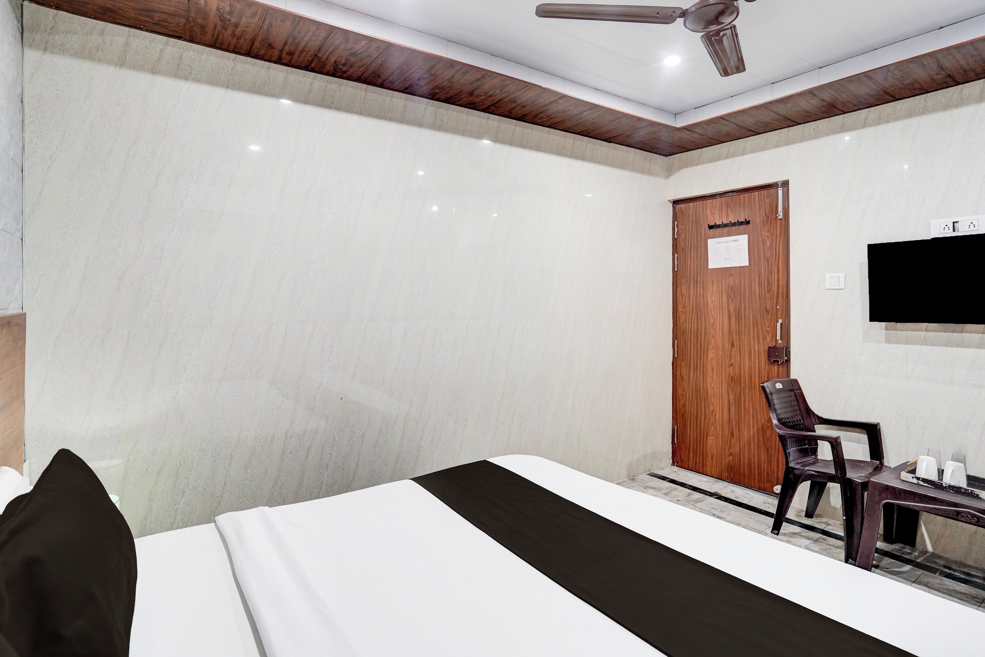 Quarto de hotel com uma cama, escrivaninha, cadeira, porta de madeira e televisão de tela plana na parede.