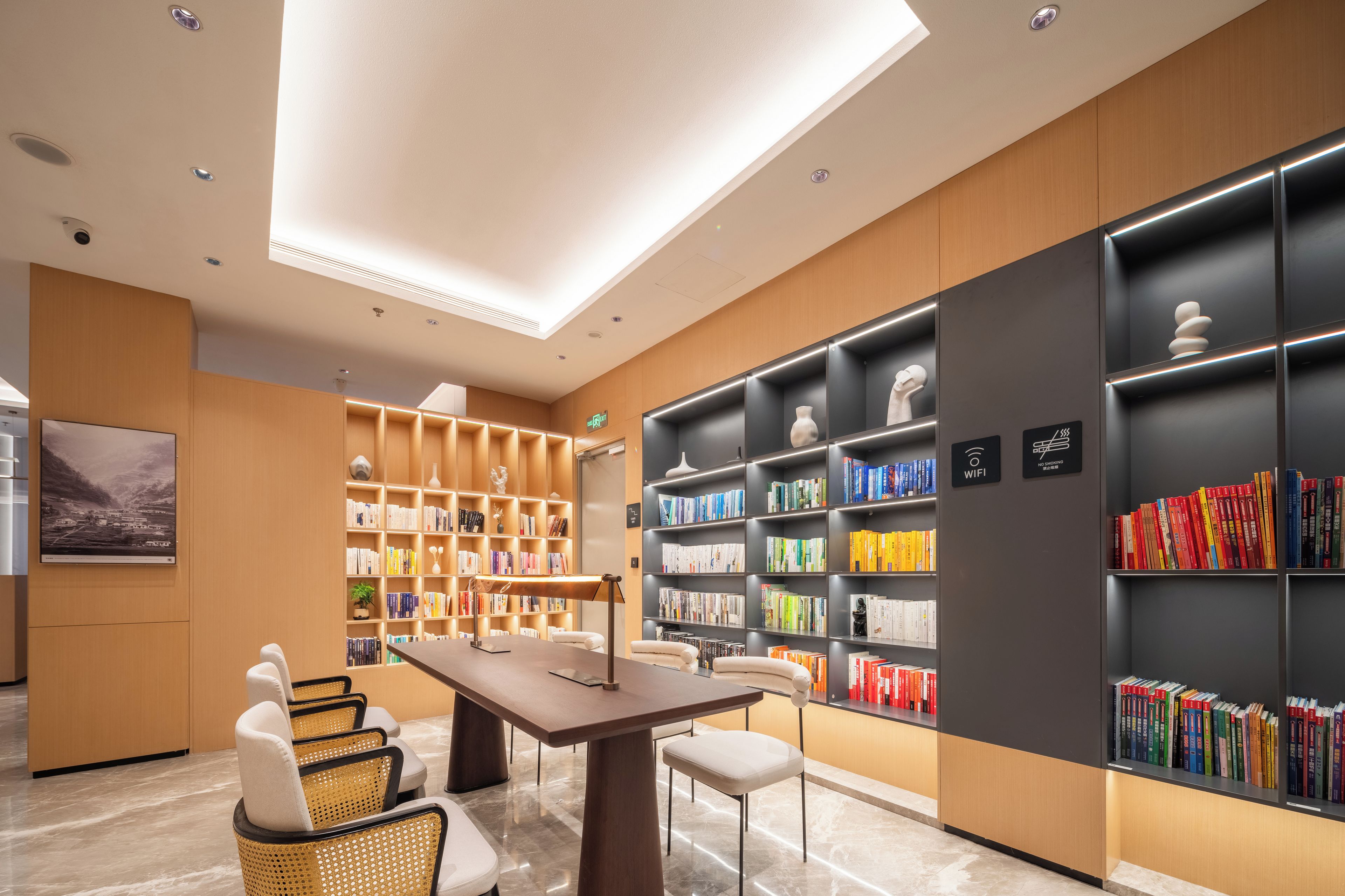 Uma biblioteca moderna com estantes, uma mesa, cadeiras e uma luminária no teto.