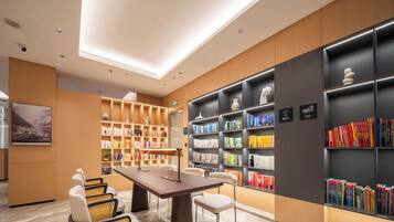 Uma biblioteca moderna com estantes, uma mesa, cadeiras e uma luminária no teto.