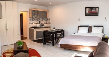 Quarto de hotel moderno com uma cama, uma pequena mesa de jantar e uma cozinha compacta.