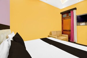 Quarto de hotel com cama, cadeira, televisão e janela com cortinas.