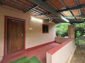 Varanda coberta com porta de madeira identificada como 'F3 FAMILY COTTAGE', uma pequena janela e uma parede de tijolos vermelhos.
