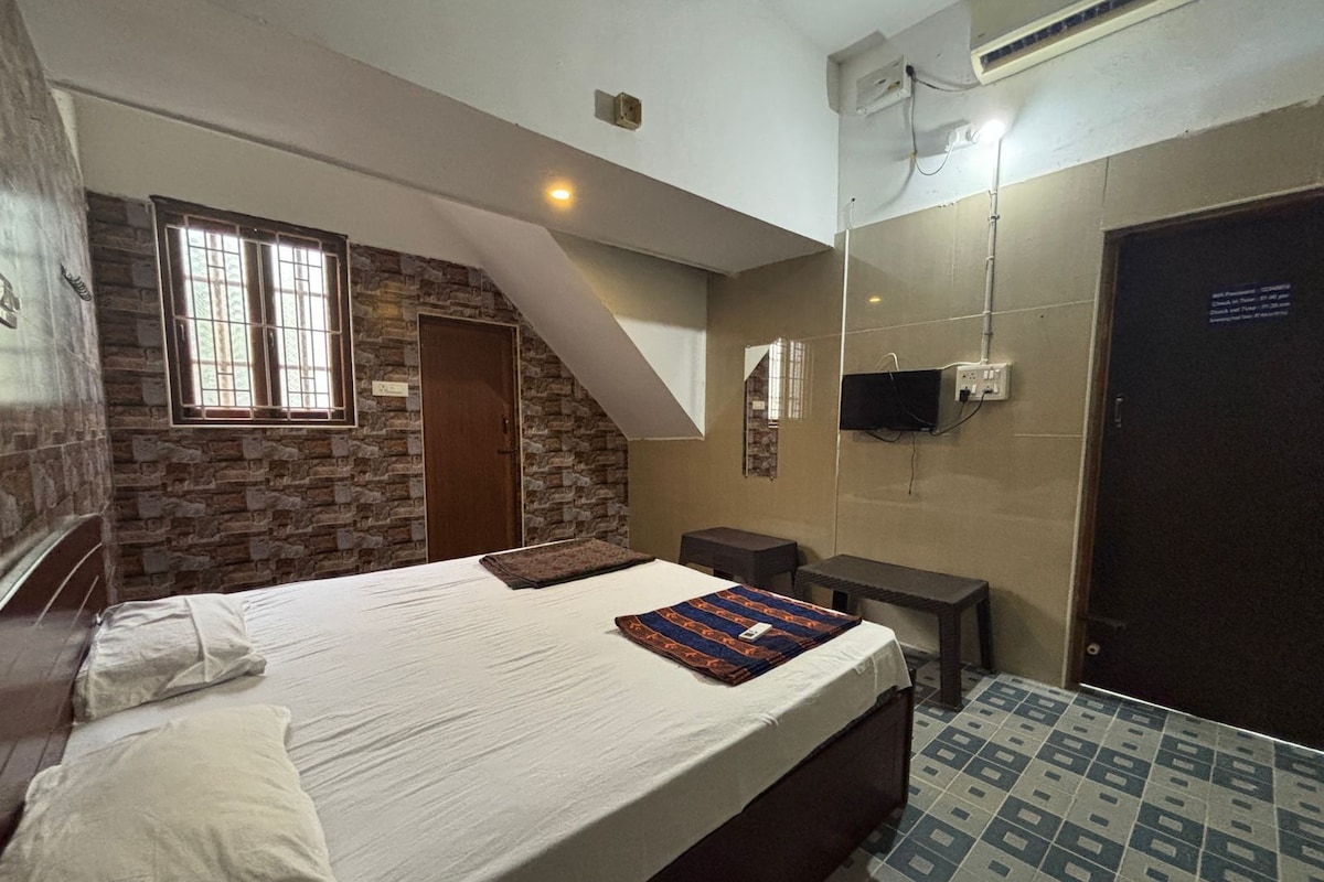 Quarto com cama, mesinha, um banco, janela e porta.