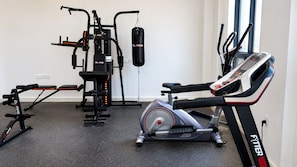 Uma academia com bicicleta ergométrica, banco de musculação e saco de pancadas.