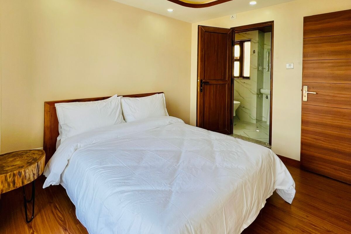 Quarto com uma cama grande, piso de madeira, porta de madeira e uma pequena mesa de cabeceira.