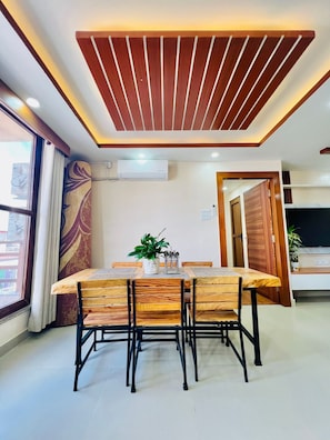 Uma área de refeições com mesa e cadeiras de madeira, um aparelho de ar condicionado e um painel decorativo na parede.