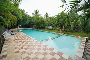 Piscina com piso xadrez, rodeada por vegetação exuberante e palmeiras.