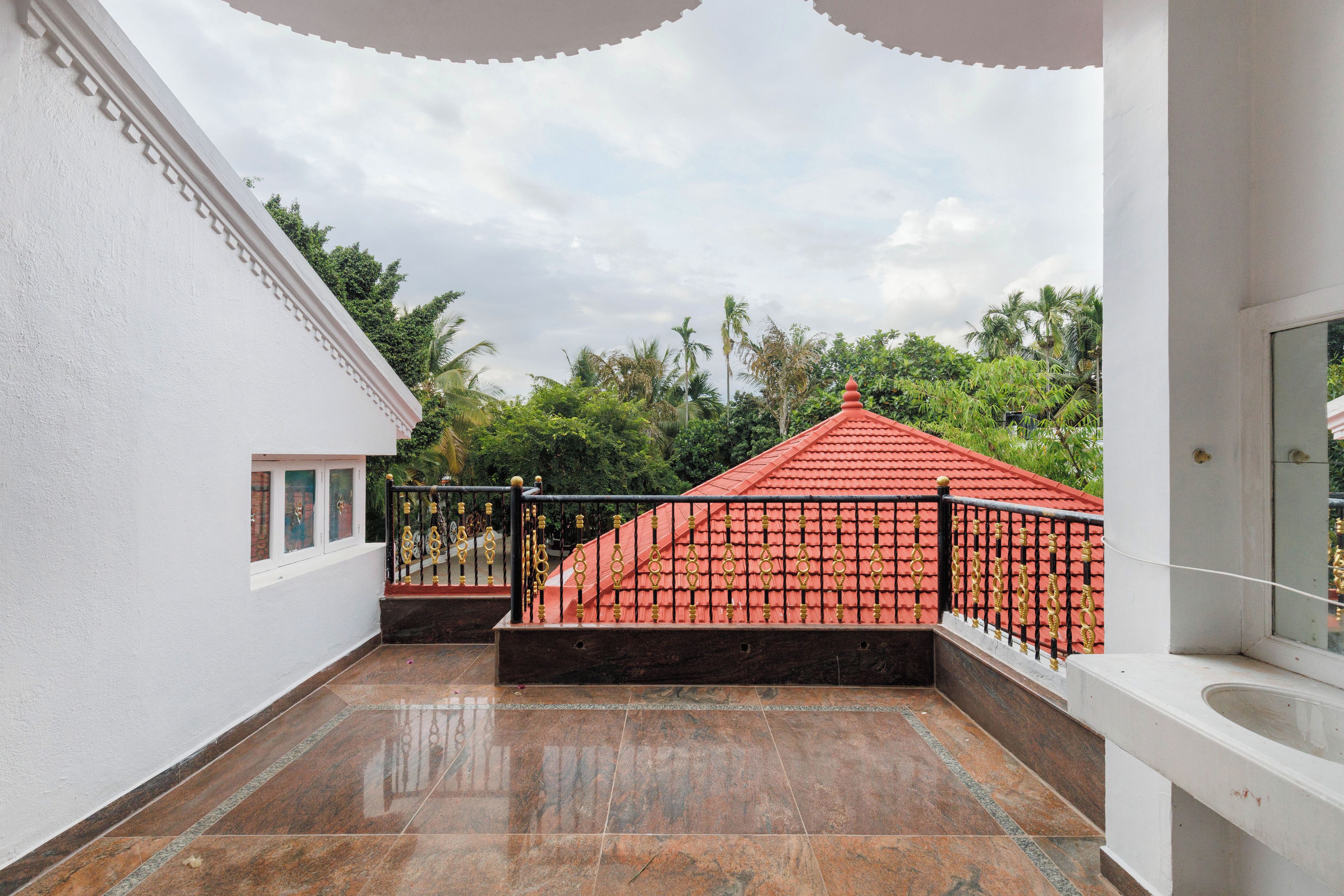 Uma varanda com uma estrutura de telhado vermelho, uma parede branca e chão de azulejos.
