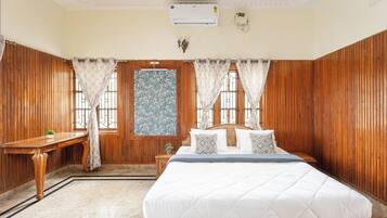 Quarto com parede de painel de madeira, cama com roupa de cama branca, uma mesinha com uma planta e uma janela com cortinas.