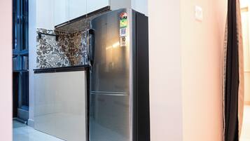 Uma geladeira de aço inoxidável com visor digital e adesivo de código de barras, colocada em um corredor com papel de parede estampado e uma porta com janela.