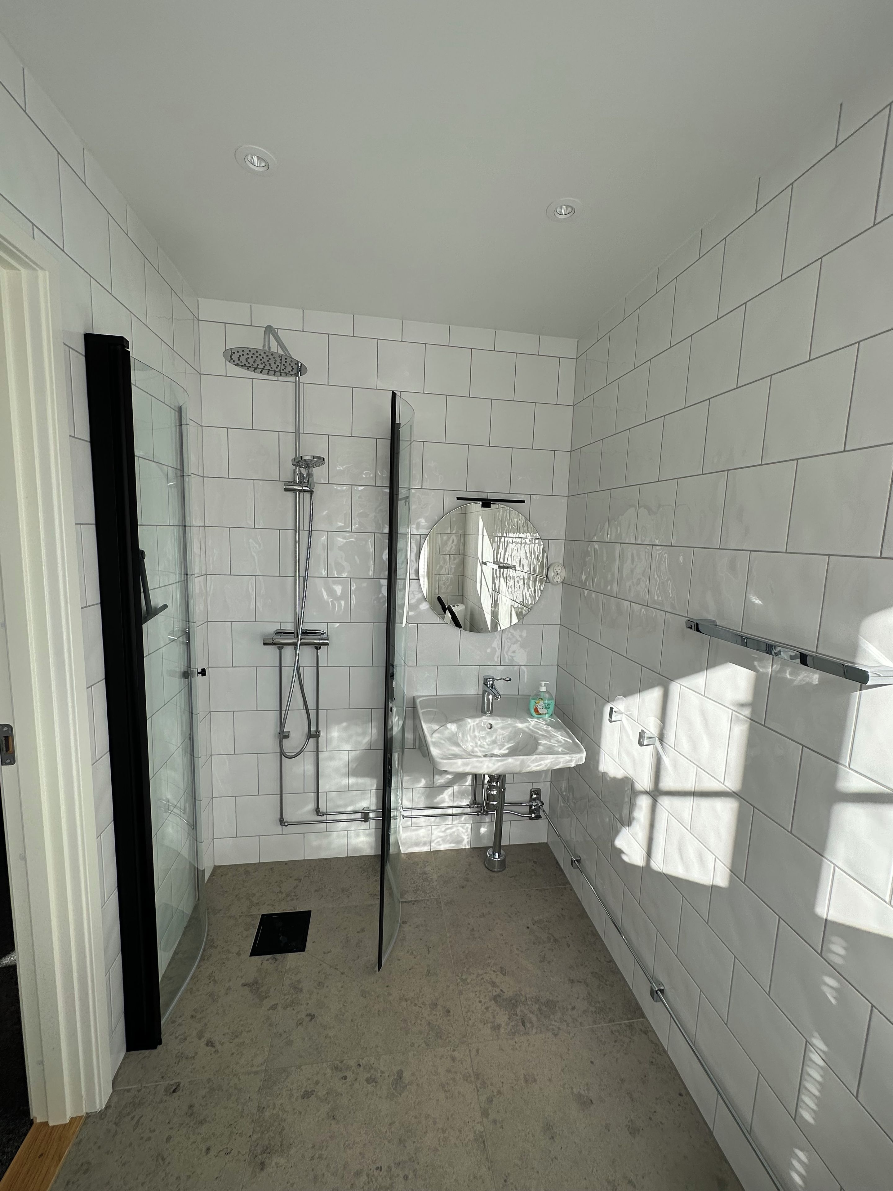 Casa de banho moderna com azulejos brancos, cabine de duche com vidro, lavatório com espelho e suporte para toalhas.
