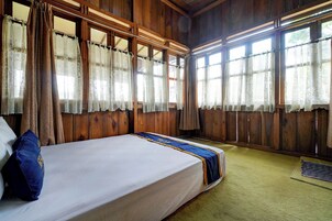 Quarto com cama grande, paredes de madeira e várias janelas com cortinas.