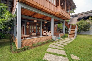 Uma casa de madeira de dois andares com varanda coberta, fachada de tijolos e um caminho de pedras até a entrada.