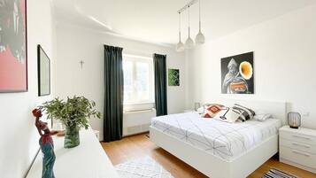 Quarto moderno com uma cama grande, mesas de cabeceira, escrivaninha e janela com cortinas.