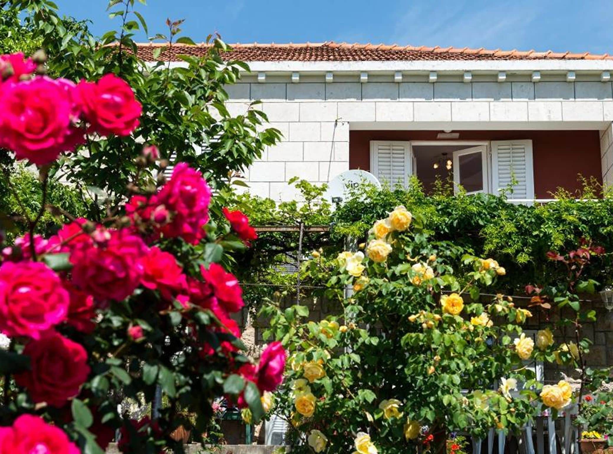 Um edifício com fachada branca, telhado telhado e um jardim com rosas rosa e amarelas.