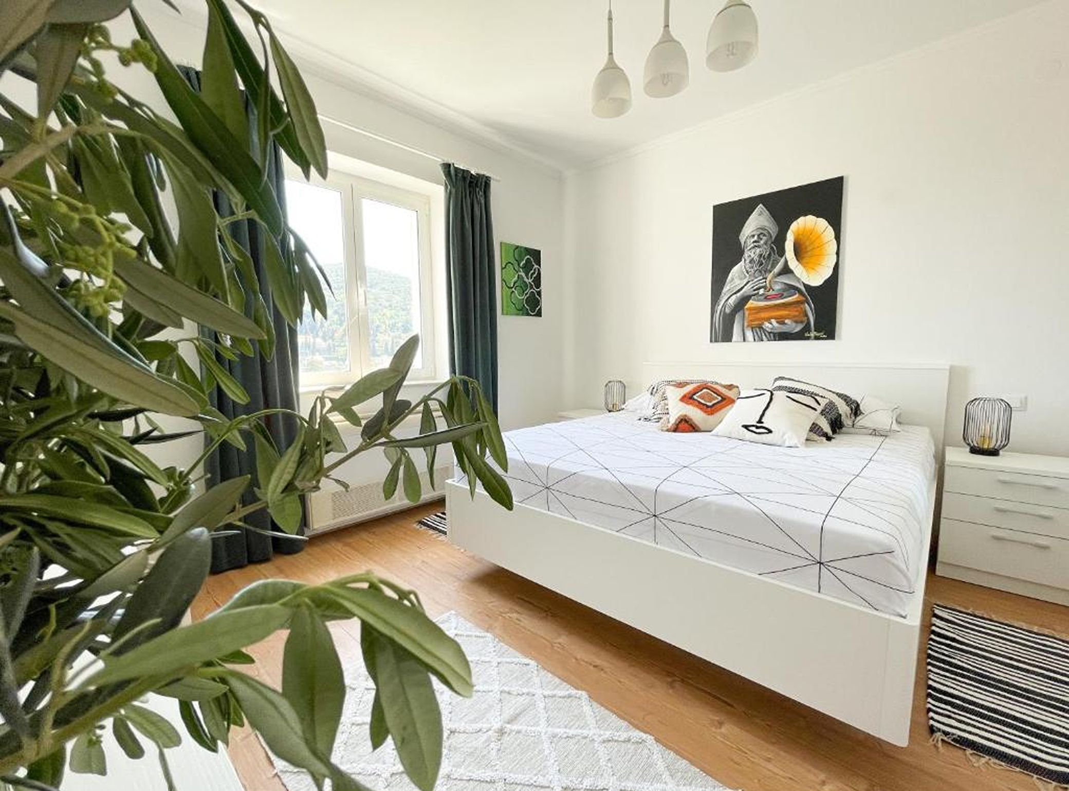 Quarto moderno com cama, mesas de cabeceira, janela com cortinas e um quadro na parede.