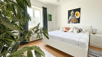 Quarto moderno com cama, mesas de cabeceira, janela com cortinas e um quadro na parede.