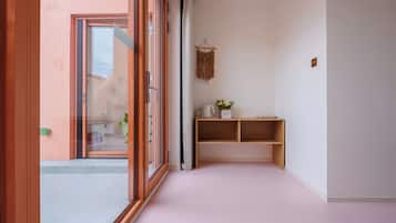 Corredor com porta de vidro deslizante que dá para área externa, banco de madeira com mesa pequena e decoração de macramê pendente, além de parede branca com interruptor de luz.