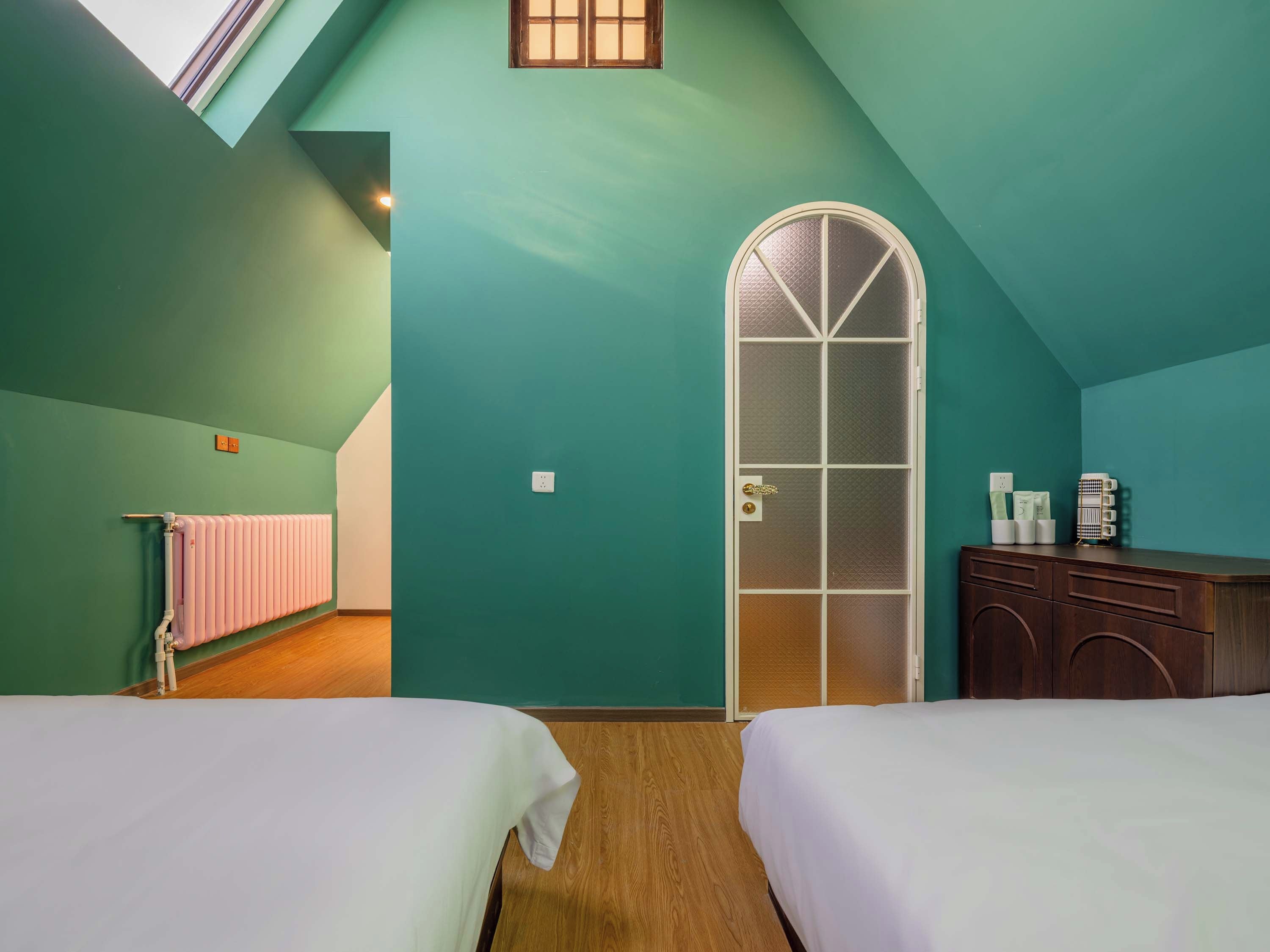 Quarto com duas camas, um radiador, cômoda de madeira e claraboia.