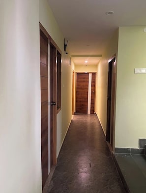 Um corredor com portas de madeira, chão de azulejos e um interruptor na parede.